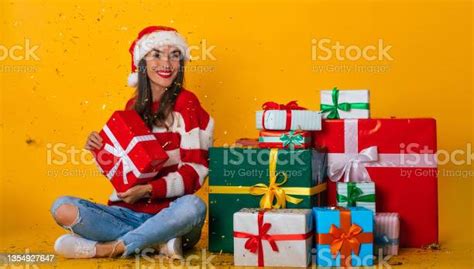 그녀는 많은 다채로운 선물 상자와 함께 앉아 색종이와 재미를하는 동안 산타 모자와 크리스마스 분위기와 함께 아름답고 매력적인 여자의 흥분 젊은 미소의 전체 길이 사진 12
