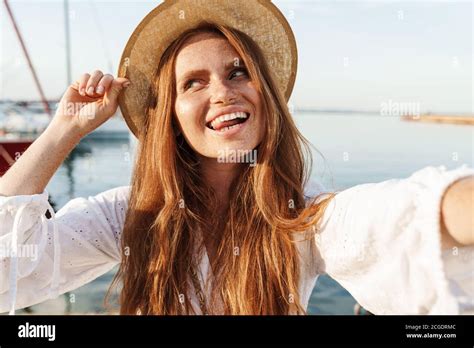 Bild von fröhlichen Ingwer Frau zeigt Zunge und Selfie Foto beim Spaziergang auf der Promenade