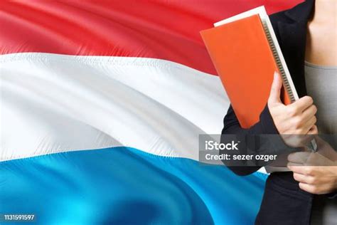 룩셈부르크 언어 개념을 학습 백그라운드에서 룩셈부르크 국기와 함께 서 있는 젊은 여자 책을 들고 교사 오렌지 빈 책 표지