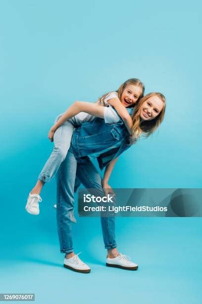 파란색에 카메라를보면서 데님 조끼와 청바지 피기 백킹 딸을 입은 젊은 여성의 전체 길이 보기 어머니에 대한 스톡 사진 및 기타 이미지 Istock