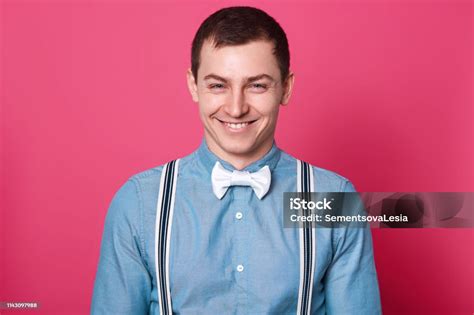 웃 고 재미 있는 남자가 카메라 앞에 똑바로 서 서 교활한 명랑 한 표현을 제공 합니다 Sprightly 졸리 젊은 남자는 블루 셔츠 흰색 나비 넥타이 낭비를 착용 합니다