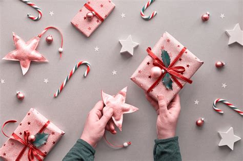 장난감 별을 들고 두 손은 선물 을 포장 분홍색 선물 상자 줄무늬 사탕 지팡이 장신구 및 장식 별 회색 종이에 기하학적 창조적 인 평면 레이아웃축제 크리스마스 배경 12월에