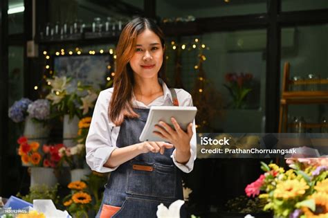 앞치마에 미소 짓는 여성 중소 기업 꽃 가게 주인이 디지털 태블릿을 들고 카메라를 보면서 꽃집 주인에 대한 스톡 사진 및 기타 이미지 꽃집 주인 태블릿 20 24세