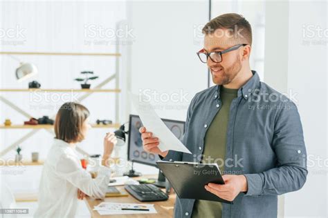 테이블 옆에 앉아있는 여자 앞에 서있는 긍정적 인 남자 사무실에서 함께 일하는 두 명의 디자이너 사무실에 대한 스톡 사진 및 기타 이미지 Istock