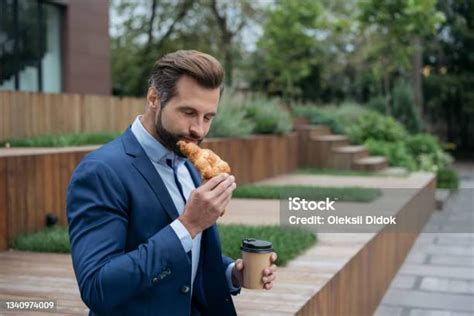 커피 한 잔을 들고 거리에서 크루아상을 먹는 사업가 행복한 수염을 기리는 남자 공원 점심 시간 커피 브레이크 컨셉에 앉아 맛있는 음식을 들고 남자 사업가에 대한 스톡 사진