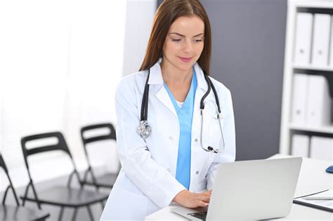 직장에서 의사 여자입니다 클리닉 또는 응급 병원 리셉션 데스크 근처에 서 있는 동안 랩톱 컴퓨터를 사용 하는 여성 의사의 초상화