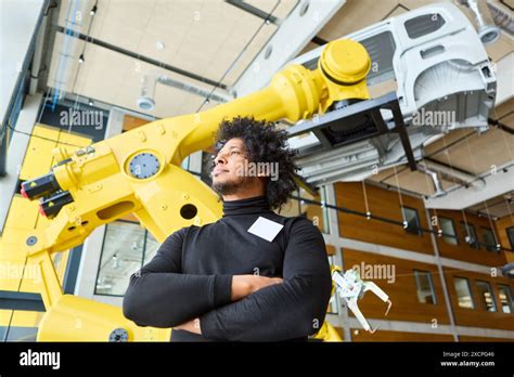 Engineer Supervising A Large Yellow Robotic Arm Used For Process Automation In An Industrial