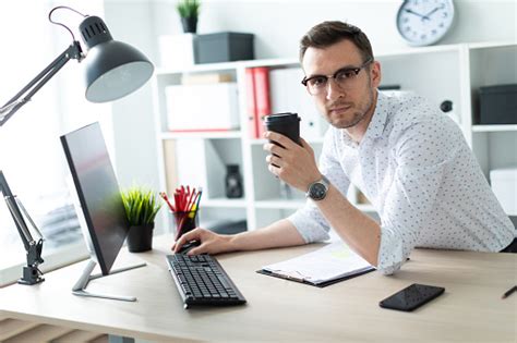 안경에 젊은 남자 근처 사무실에 테이블 스탠드 그의 손에 커피 한잔을 보유 하 고 컴퓨터와 함께 작동 감독에 대한 스톡 사진 및 기타 이미지 Istock