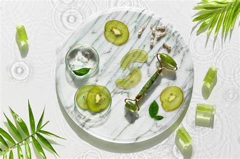화장품 스킨케어 배경 키위 슬라이스와 야자수 잎을 곁들인 허브 약품 수제 설탕 스크럽 자연 햇빛 긴 그림자 스플래시 물 원