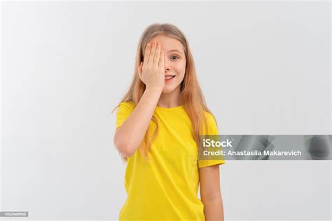 웃고 있는 십 대 소녀가 얼굴을 손바닥으로 만들고 놀란 입을 벌리고 손바닥으로 얼굴의 절반을 가리고 카메라에 한쪽 눈으로 보고 흰색 스튜디오 배경 위에 서 있다 아이에 대한