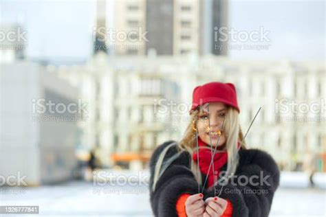 거리에서 스파클러와 함께 크리스마스를 축하하는 세련된 빨간 모자와 스카프를 입은 귀여운 금발 여성 텍스트 공간 20 24세에