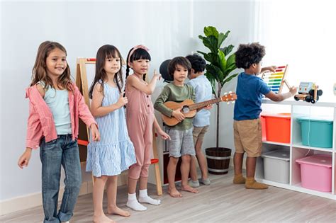 혼합 인종 어린 아이의 그룹은 학교 방에서 기타를 연주 어린이 소녀와 소년 학생은 음악을 연주하면서 노래를 부르고 춤을 추며 Schoo의 교실에서 함께 즐거운 시간을