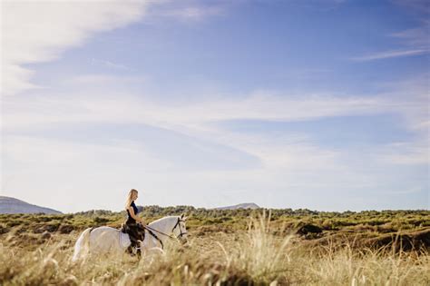 Young Blonde Woman Riding Her White Horse Through Lush Green Sand Dunes