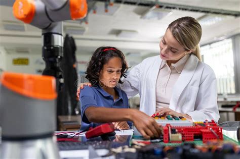 Female Teacher Helping Young Schoolboy To Build Robot Kit In After
