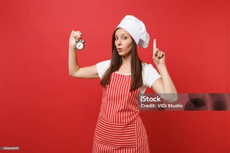 주부 여성 요리사 요리사 또는 줄무늬 앞치마 흰색 티셔츠 모자 요리사 모자 빨간 벽 배경에 고립 된 베이커 예쁜 여 자가 손 복고풍 자명종 서둘러 개최 복사 공간 개념을