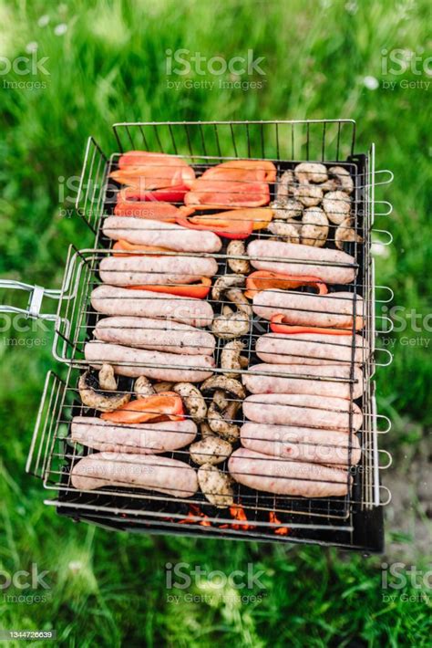 소시지에 채소와 향신료를 화로위에 구워주세요 맨 위 보기입니다 바베큐 그릴에 훈제와 불꽃이 있는 다양한 맛있는 구운 고기가 녹색 잔디에 있습니다 꼭대기에 대한 스톡 사진 및