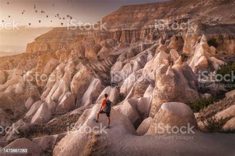 남성 여행자는 카파도키아 투르 키예 의 다양한 원뿔 모양의 지질 학적 형성물과 일몰시 배경에 날아 다니는 풍선 그룹을 존경합니다 괴레메에 대한 스톡 사진 및 기타 이미지