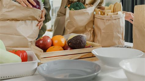 식료품 가방을 들고 슈퍼마켓에서 도착하고 집에서 부엌에서 포장을 푸는 젊은 아시아 여성 친구들의 클로즈업 자연 생활을 즐기는 건강 한 음식을 먹는 라이프 스타일 가정 생활에