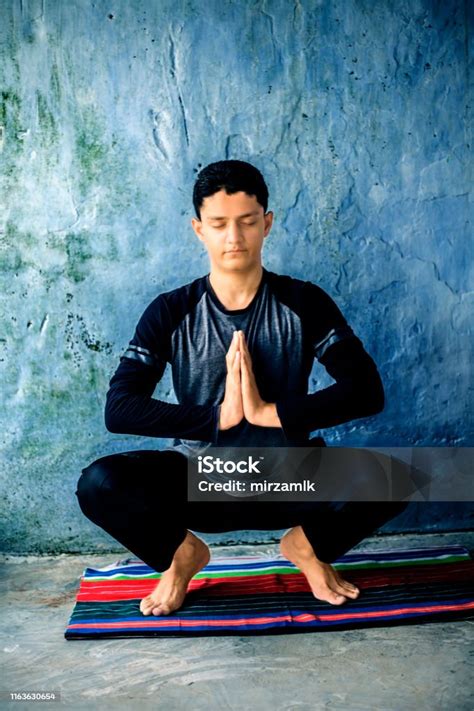 검은 색 의상을 입고 화려한 전통 매트에 요가를하고 유명한 갈랜드 포즈 또는 말라사나일을하는 십대 소년 수직 샷 Malasana Yoga에 대한 스톡 사진 및 기타