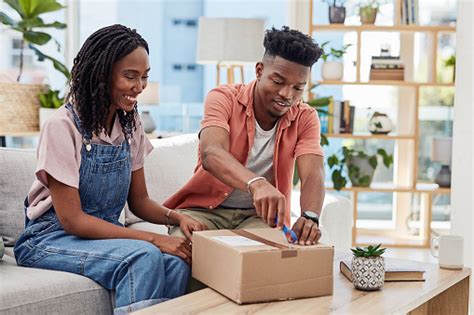 상자를 열고 행복하고 배달 전자 상거래 패키지 및 집 소포를 가진 흑인 커플 흥분한 물류와 아프리카 남자와 여자가 거실에서 제품을 위해 함께 선적을 자르고 있습니다 배달에