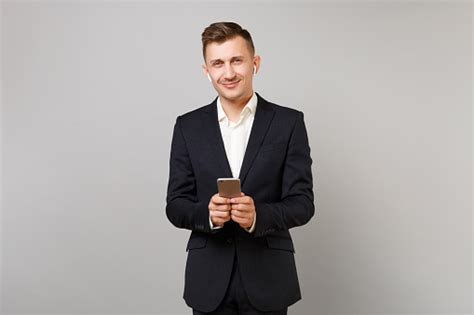젊은 사업가 음악 휴대 전화를 사용 하 여 무선 이어폰 웃 고 회색 배경에 고립 Sms 메시지를 입력 성과 경력 부 비즈니스 개념입니다 복사 공간을 비웃는 다 검은색에 대한