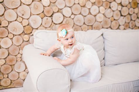 작은 파란 눈 여 자가 삼 베의 형태로 장식 나무 벽을 가진 방에 있는 베이지색 소파에 기 뻐 하 고 그녀의 머리에 장식 된 흰 디자이너 드레스에 금발 귀여운에 대한 스톡