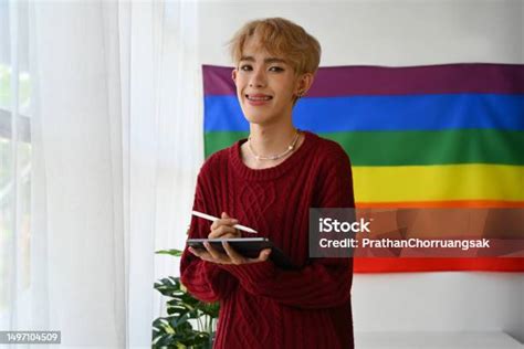 무지개 프라이드 깃발이 있는 밝은 거실에서 디지털 태블릿을 사용하는 쾌활한 십대 게이 남자 Lgbtq 가정 생활 및 기술 18 19세에 대한 스톡 사진 및 기타 이미지