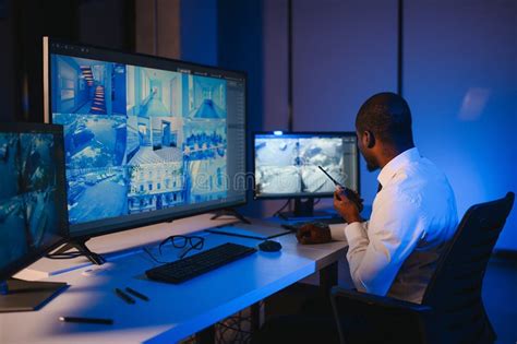 African American Security Officer Or Dispatch Uses Computer And Walkie Talkie Looks At Screens