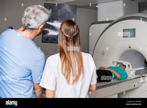 Doctors Analyzing X Ray With Patient Lying On Mri Scan Machine In