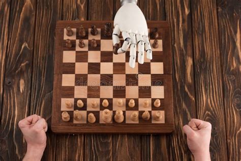 cropped shot of robot playing chess with human on wooden surface stock