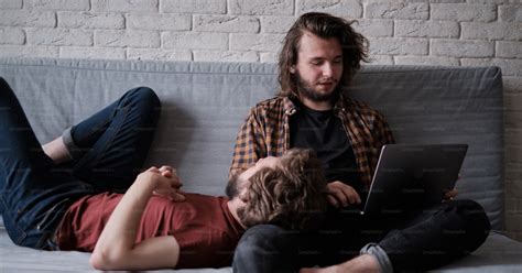 소파에 누워 휴식을 취하고 함께 시간을 보내는 두 명의 중년 수염 난 남자의 초상화 하나는 노트북을 사용하고 있습니다 사진 Unsplash의 성인 이미지