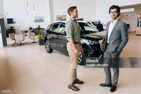 자동차 대리점에서 수염을 기른 남성 고객과 함께 차량의 사양과 성능에 대해 이야기하는 전문 남성 자동차 판매자의 전체 길이
