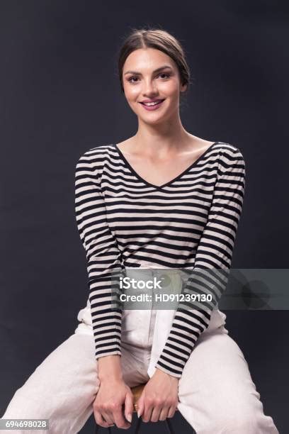 한 젊은 백인 여자 20 대 2029 년 패션 모델의 자 바에 앉아 웃 고 포즈 스튜디오 흰색 배경 가로 스트라이프 셔츠 흰색 바지 카메라를 보고 20 29세에 대한 스톡