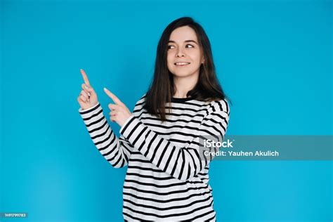 줄무늬 풀오버를 입은 사랑스러운 소녀가 빈 공간을 가리키고 응시하고 있다 표현적인 제스처를 가진 매력적인 젊은 여성 모델 파란색