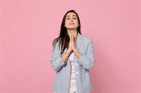 함께 손을 잡고와 스튜디오에서 분홍색 파스텔 벽 배경에 고립 기도하는 줄무늬 재킷에 탄 원 젊은 여자의 초상화 사람들은 진심으로 감정 라이프 스타일 개념입니다 복사 공간을