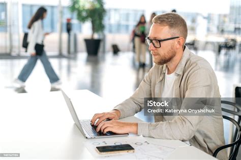 안경을 쓰고 캐주얼 한 세련된 옷 It 전문가 개발자 프로그래머 사무실에서 새로운 프로젝트에서 노트북으로 작업하고 새로운 프로그램을 개발하는 성공적인 동기 부여 백인 남자