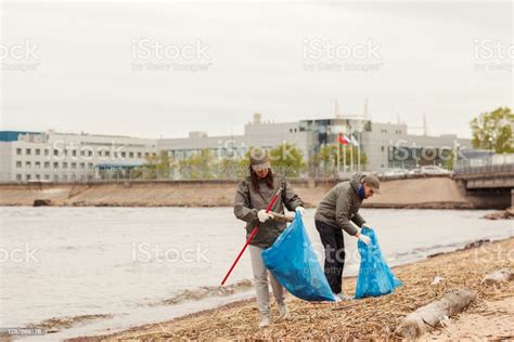 쓰레기 피커와 비닐 봉지를 사용하여 바다 해안을 청소하는 두 명의 젊은 환경 자원 봉사자 남자와 여자 30 34세에 대한 스톡