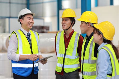 보호복을 입은 기술자 엔지니어와 사업가 그룹이 서서 산업 제조 공장에서 태블릿과 함께 토론하고 연구하고 브레인스토밍하고 계획을