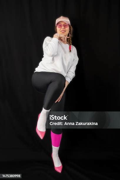 검은 배경에 고립된 트렌디한 옷을 입은 젊은 여자 흰색 스웨트 셔츠 검은 색 레깅스 흰색 양말 분홍색 발 뒤꿈치 신발을 신고