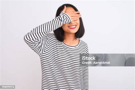 줄무늬 티셔츠를 입은 젊은 중국 여성이 고립된 흰색 배경 위에 서서 미소를 지으며 눈을 가린 얼굴을 보며 웃고 있습니다 블라인드 개념 T 셔츠에 대한 스톡 사진 및 기타