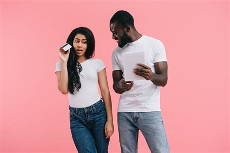 매력적인 아프리카계 미국인 여자 보여주는 신용 카드 동안 그녀의 남자 친구가 근처에 서 분홍색 배경에 고립 Brand Name Mobile Payment에 대한 스톡 사진