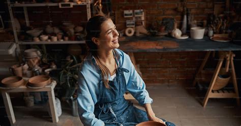 앞치마를 입은 긍정적인 공예 여성은 아트 스튜디오에서 세라믹 그릇을 제조하는 동안 시선을 돌리면서 도자기 바퀴 근처에 앉아 있다 사진 Unsplash의 손가락 이미지