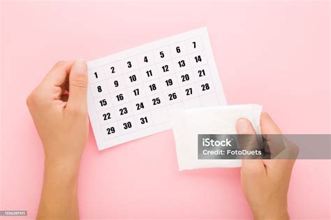 밝은 분홍색 테이블 배경에 흰색 달력과 위생 수건 팩을 들고 젊은 성인 여성 손 파스텔 색상 근접 촬영 생리 주기 관점 샷 하향