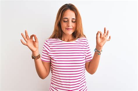 흰색 고립 된 배경에 앉아 줄무늬 캐주얼 티셔츠를 입고 젊은 빨간 머리 여자는 손가락으로 명상 제스처를하고 눈을 감고 미소 요가 개념입니다 T 셔츠에 대한 스톡 사진 및