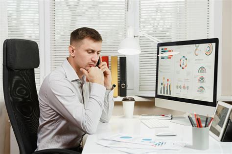 심각 하 고 몰두 비즈니스 휴대 전화에 현대 모니터 컴퓨터 문서 창 배경에 빛 사무실에서 일 얘기과 셔츠는 책상에 앉아 있는 남자 관리자 또는 작업자 합니다 사람들에 대한