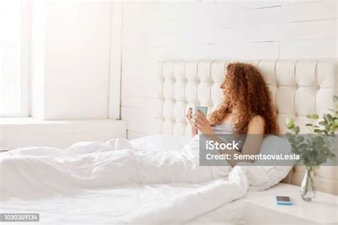 평온한 휴식 여자의 뜨거운 커피나 차 한잔과 함께 편안 하 게 침대에 앉아 넓은 백색 침실에 앉아 좋은 아침을 즐깁니다 사람 라이프 스타일 나머지 및 시작 하는 새로운 작업