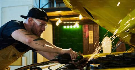 차고에서 작업하는 동안 모터의 세부 사항을 수리하기 위해 전기 그라인더를 사용하는 동안 자동차 엔진 위로 구부러진 젊은 수리공 사진 Unsplash의 자동차 이미지