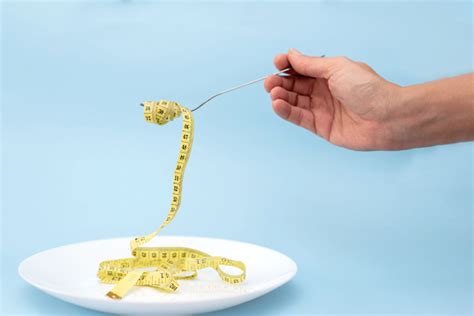 밝은 파란색 배경 식이 요법 및 영양 개념에 흰색 접시 위에 노란색 테이프를 측정하는 핸드 홀딩 포크 가냘픈에 대한 스톡 사진 및 기타 이미지 Istock