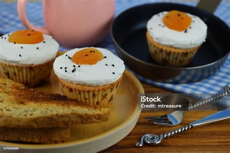 홈메이드 프라이드 에그 바닐라 컵케이크 의 이미지 종이 케이크 케이스에 흰색 파이프 착빙 프로스팅과 말린 살구를 얹고 구운 통밀 빵 삼각형 조각 배경에 분홍색 우유 주전자