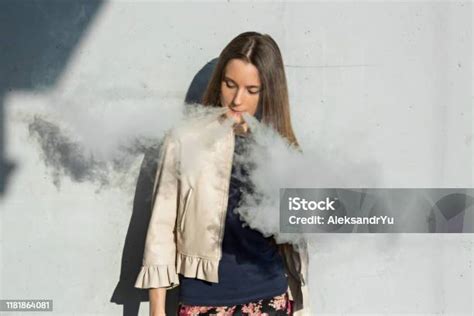 Vape 십대 캐주얼 한 옷을 입은 어린 귀여운 소녀가 여름날 야외 벽 근처에서 전자 담배를 피울 수 있습니다 나쁜 습관 18 19세에 대한 스톡 사진 및 기타 이미지